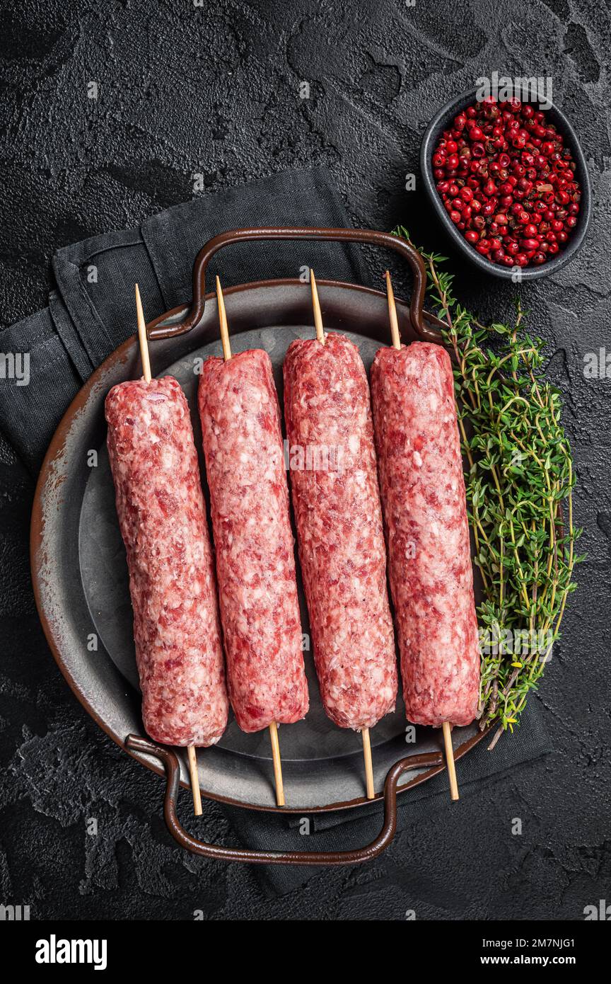 Raw Turkish Urfa kebab skewers in steel tray with herbs. Black ...