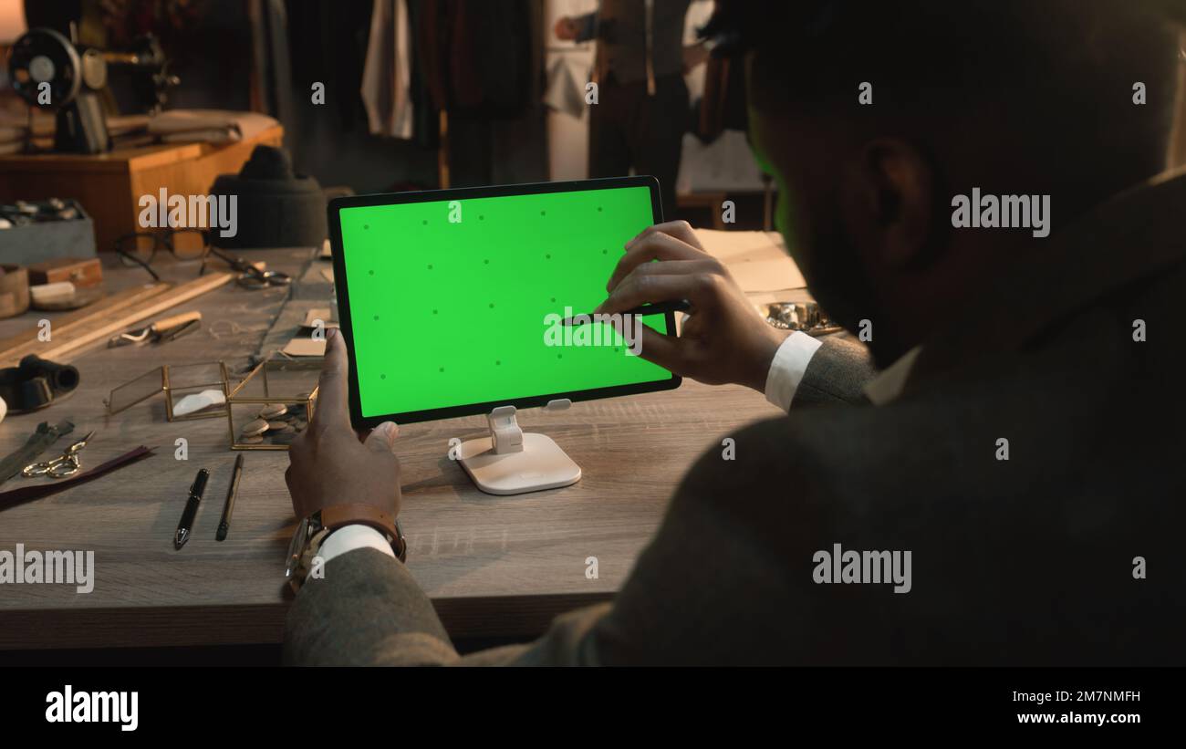 African American tailor sitting at the table in luxury atelier, surfing ...