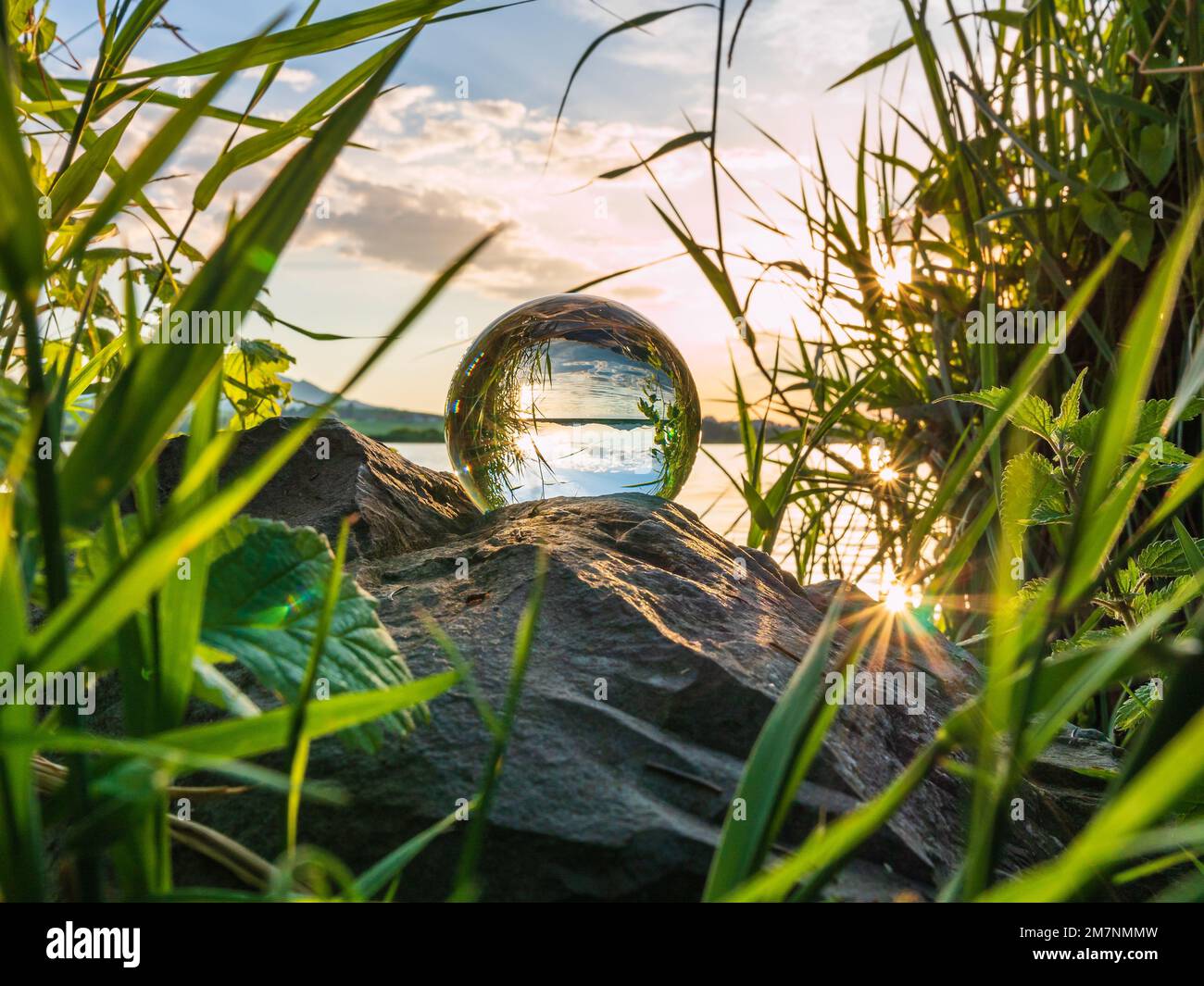 A reflecting glass ball on the beach with log grass under sunset sky ...
