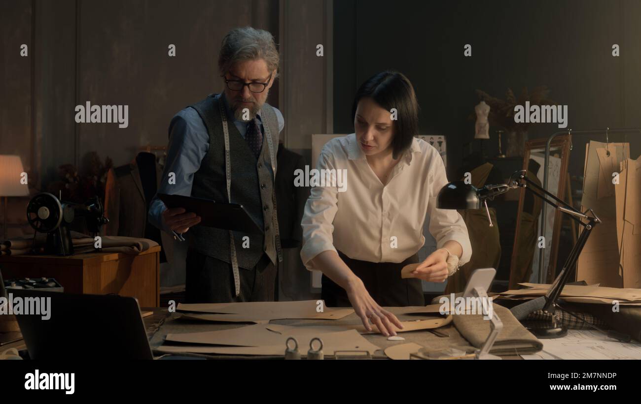 Mature tailor shows sketch of future clothes collection to seamstress ...