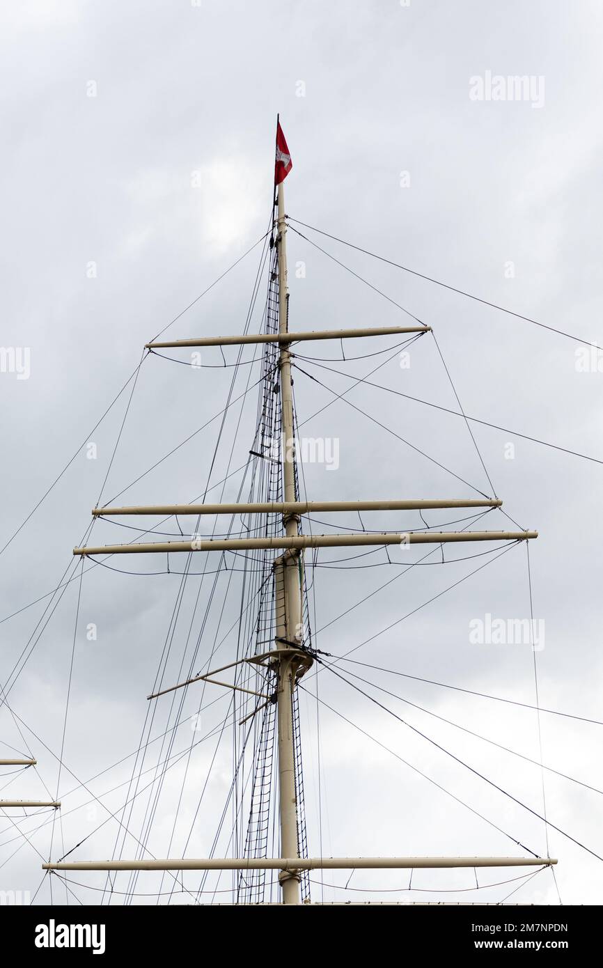 Rigging of a large sailboat with red flag in front of dark clouds in ...