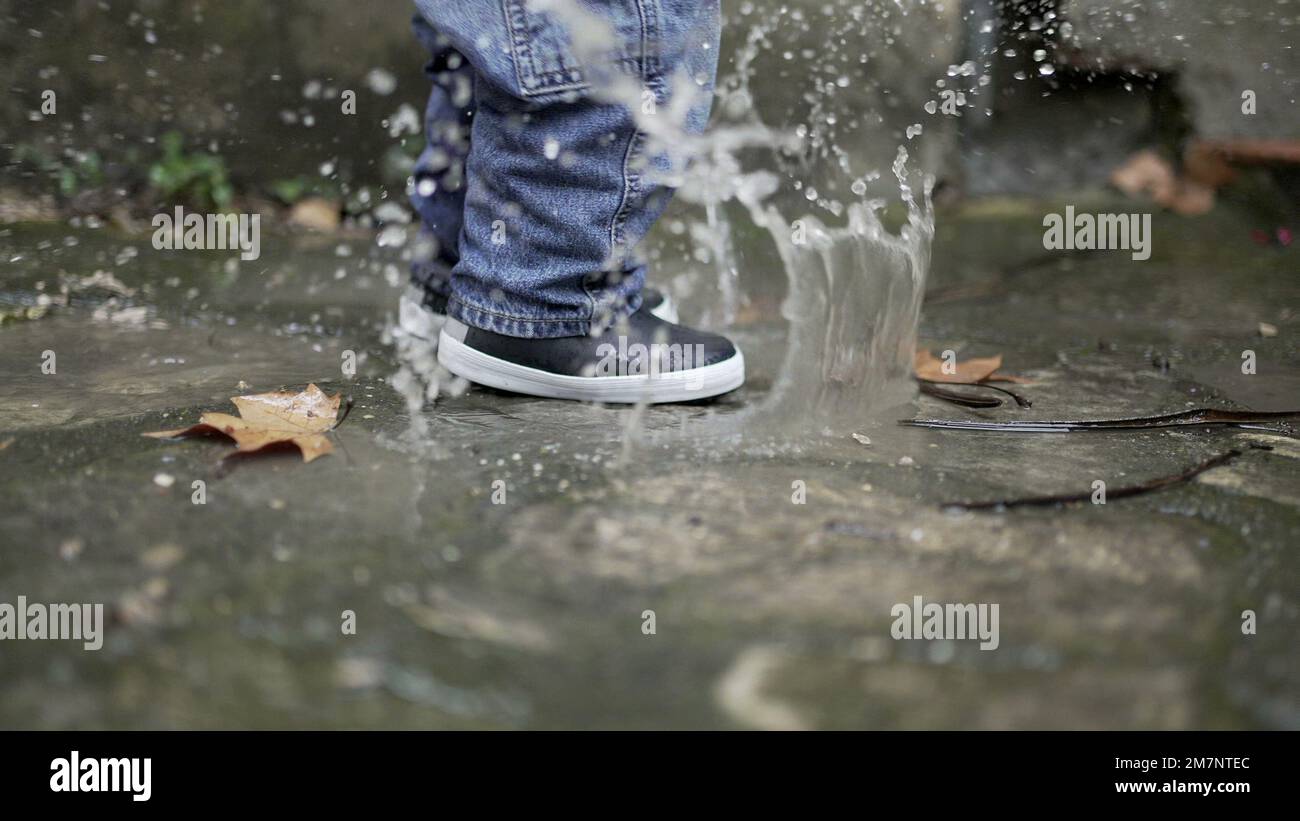 Child jumping into water puddle. Toddler wearing boots splash into ...