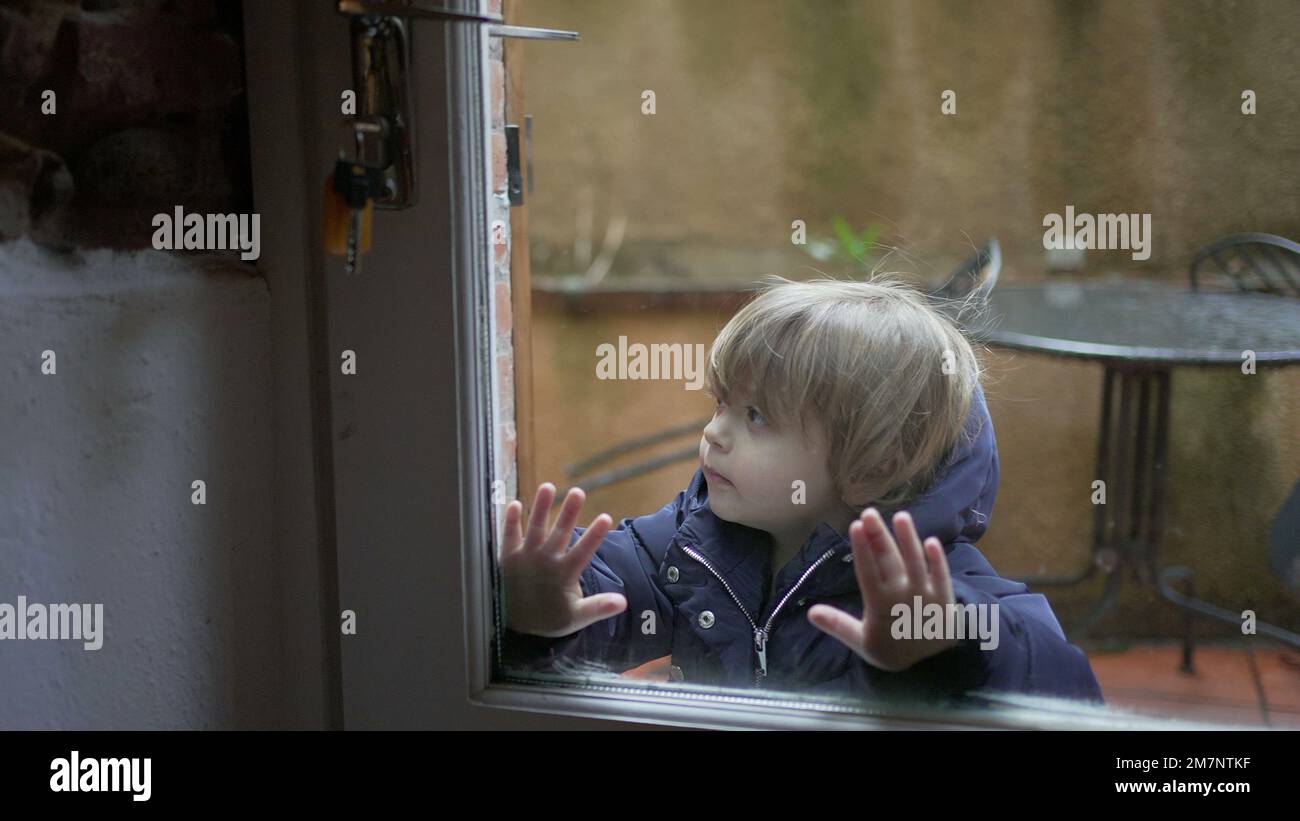 Cute baby toddler leaning on window, front entrance door Stock Photo ...