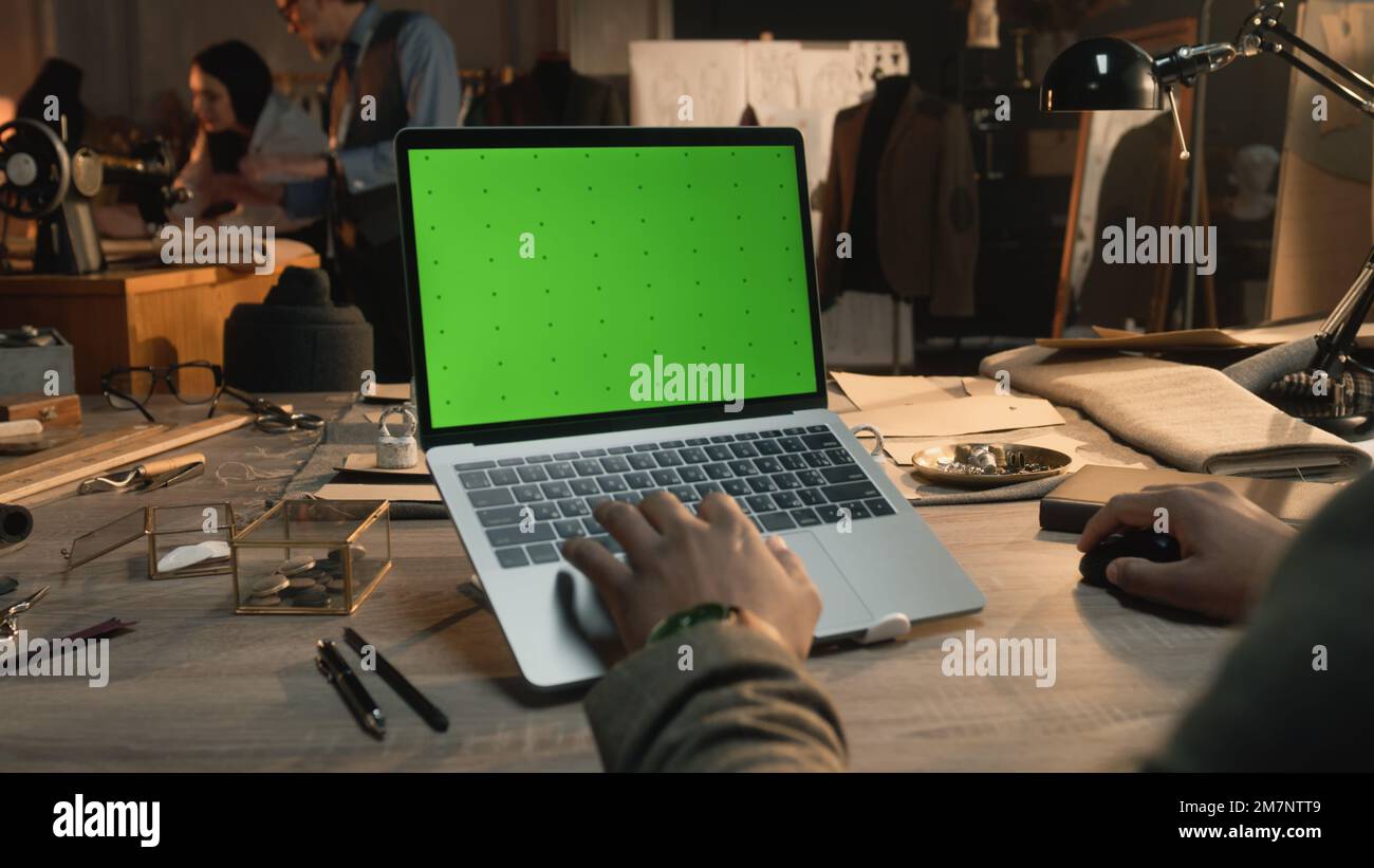 African American fashion designer sits at the table, types on keyboard ...