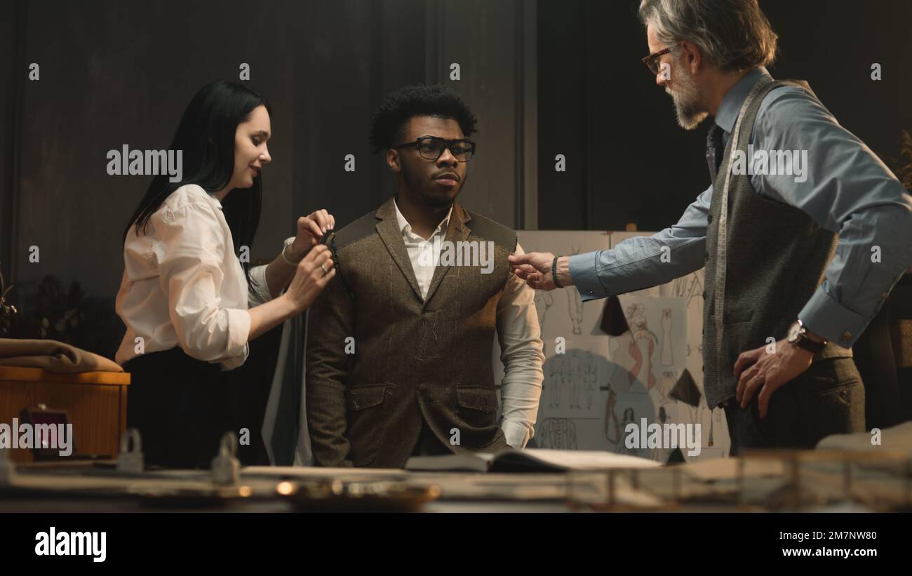 Female tailor measures sleeve of tailored suit, discusses with client ...