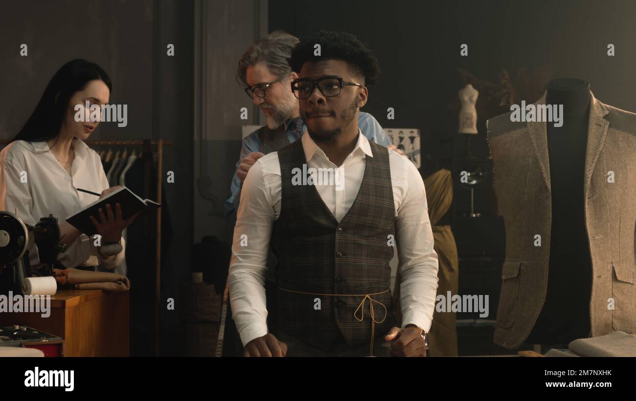 Male tailor measures African American client, discusses with female ...