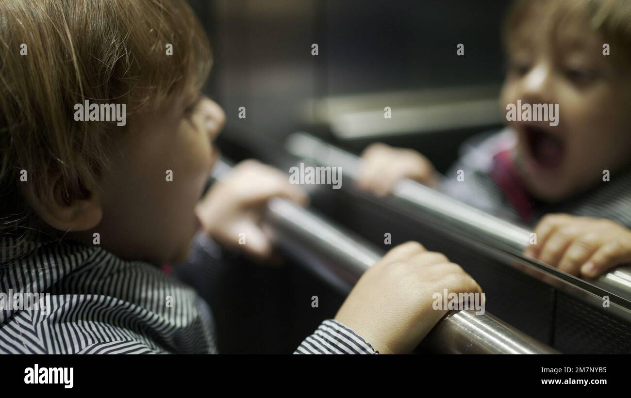 Cute baby toddler playing inside elevator staring at mirror reflection ...