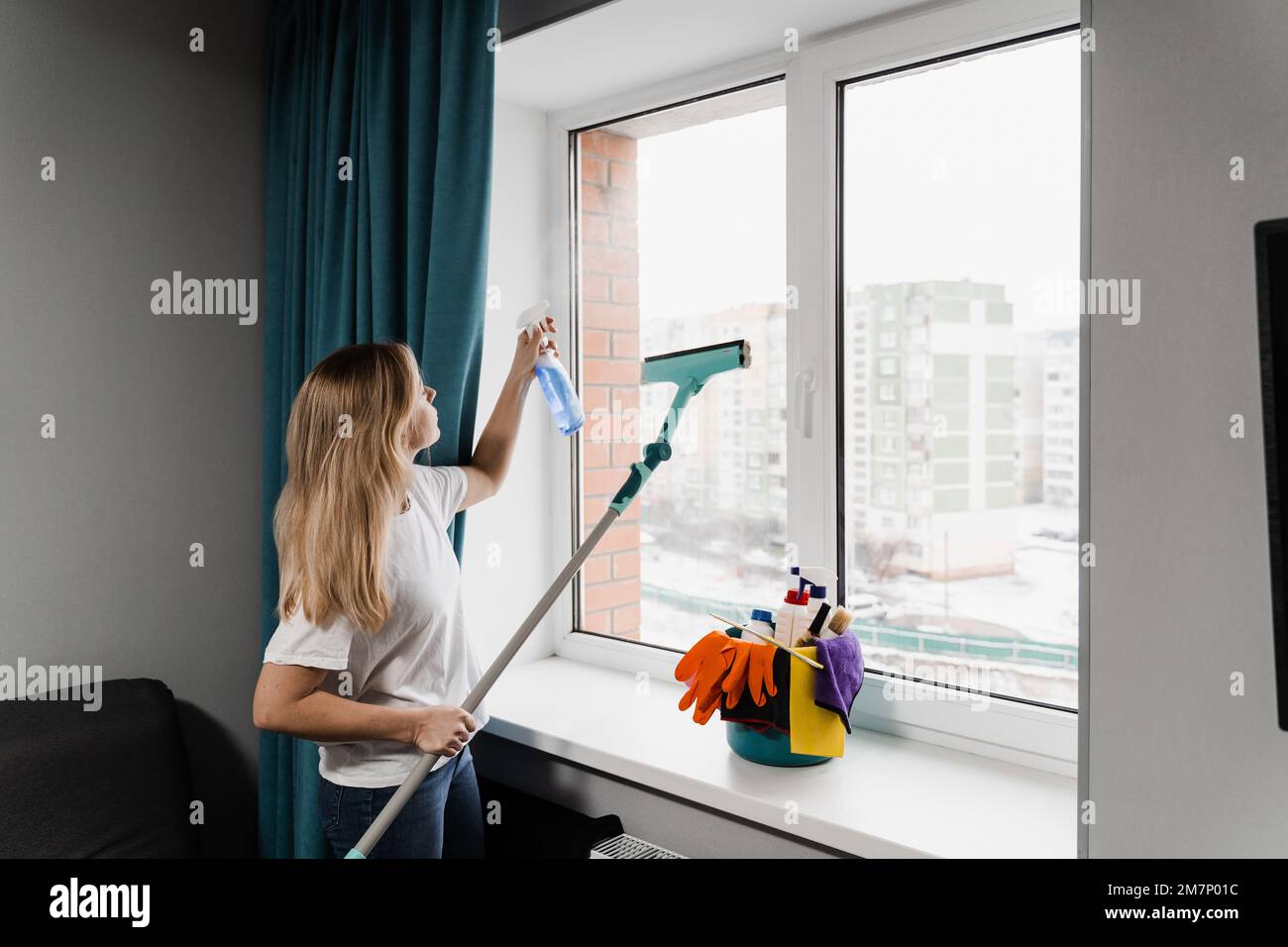 Housekeeper is spraying detergent and cleaning window at home ...