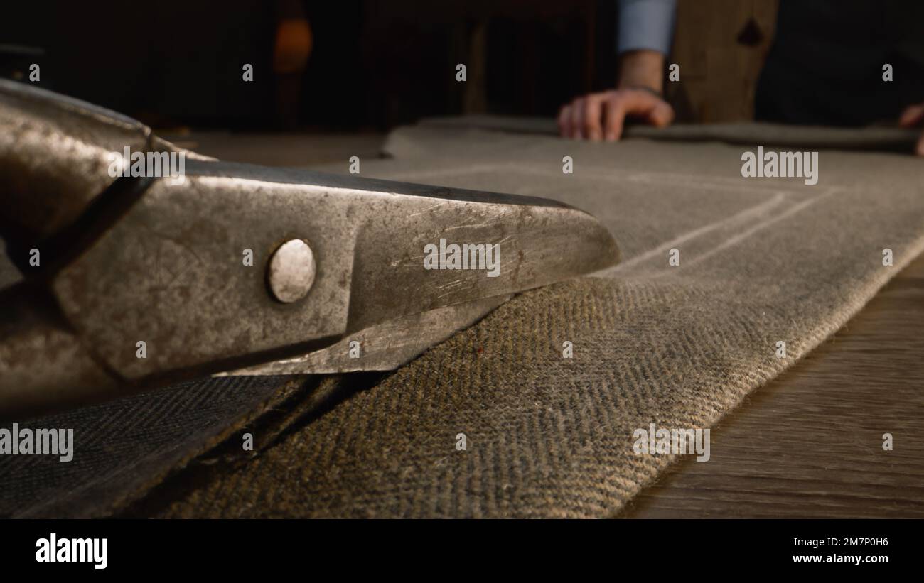 Close-up shot of tailor cutting fabric according to sketch using ...