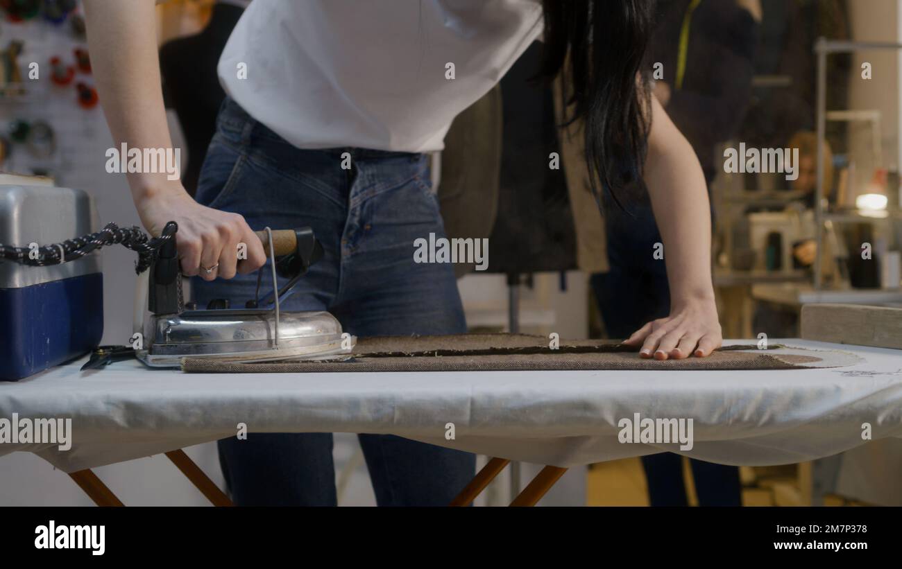 Woman irons fabric textile in atelier workshop. Her colleagues working ...