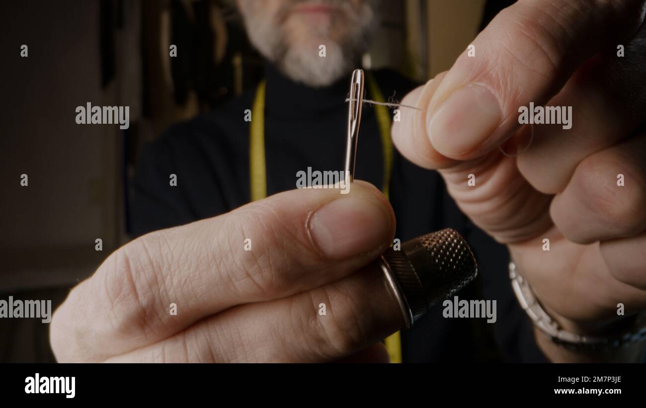 Extreme close up blurred shot with male tailor puts sewing thread in ...