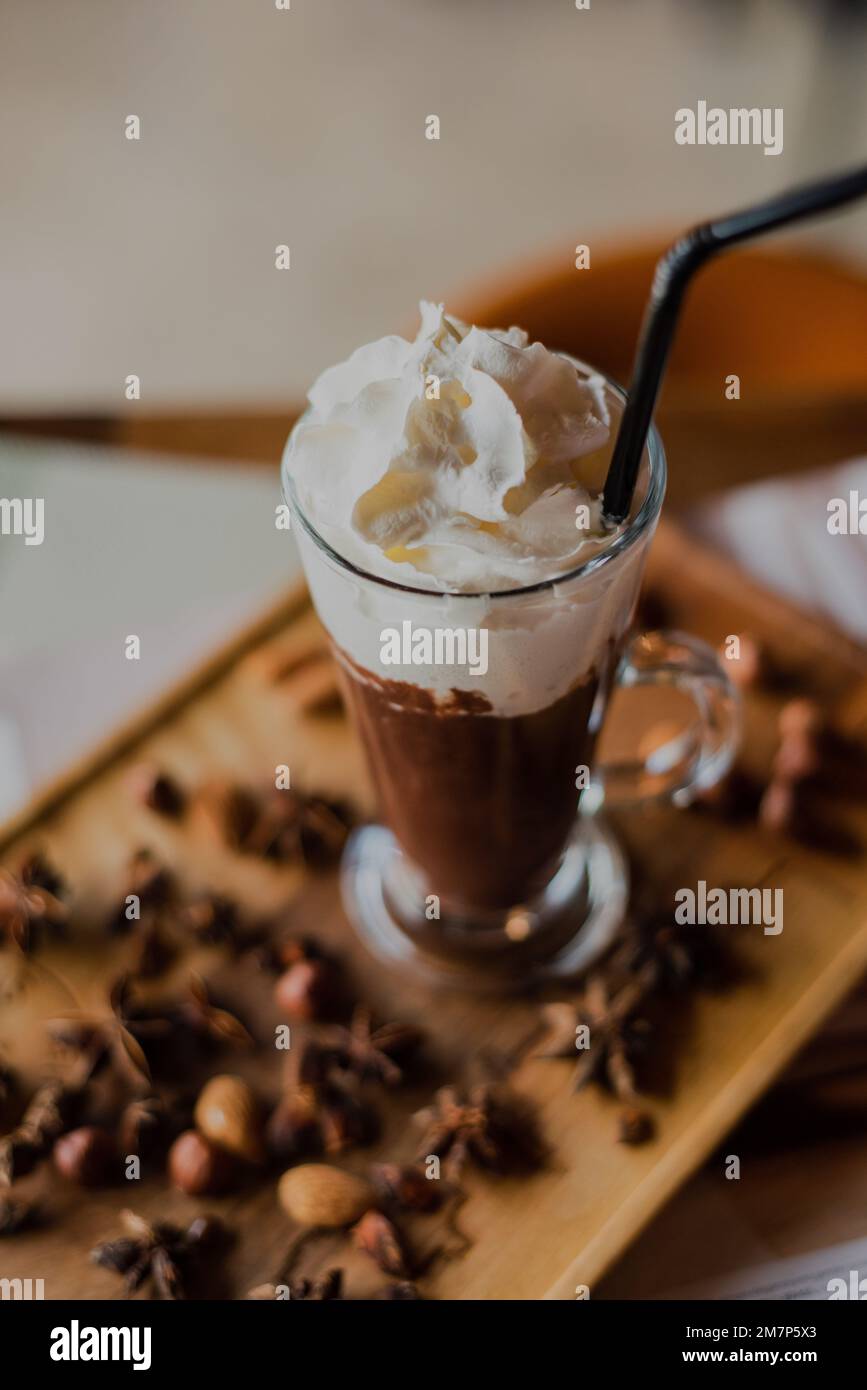 A close-up hot chocolate in a tall glass with whipped cream on a wooden ...