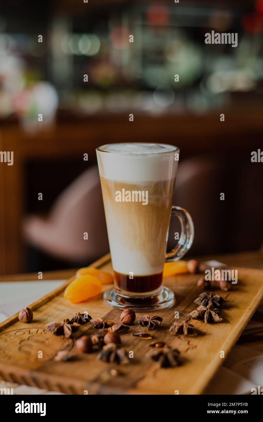 A close-up of a layered latte in a tall glass on a wooden board in a ...