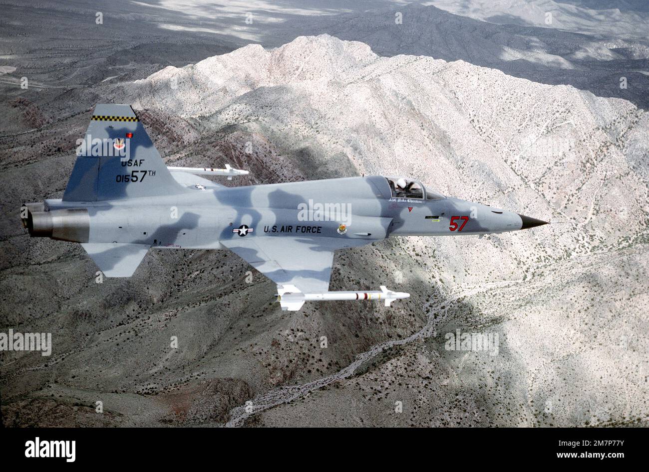A high angle right rear view of an F-5 in flight over a range. One AIM ...