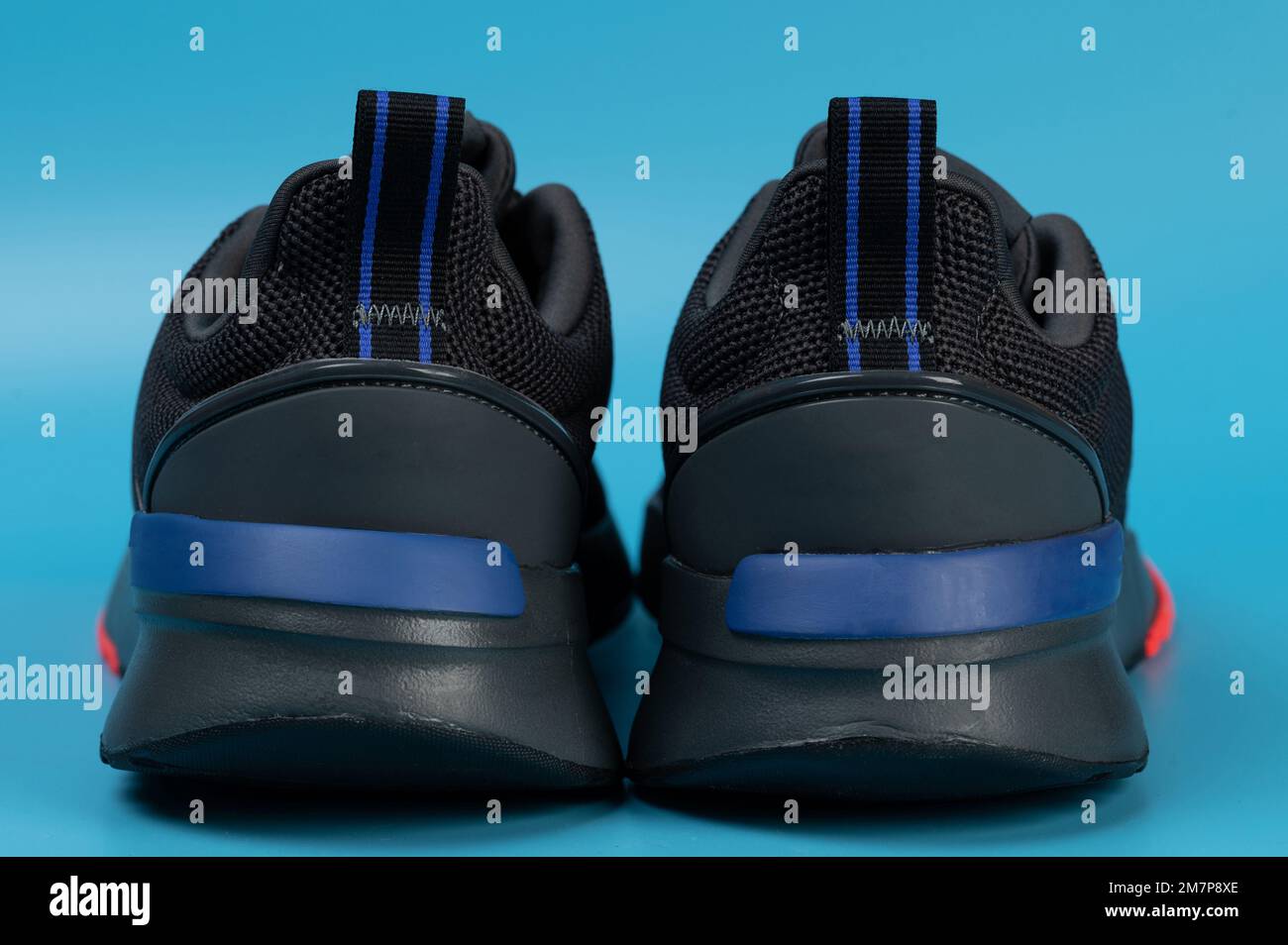 Rear view of black trainers shoes isoated on blue studio background ...