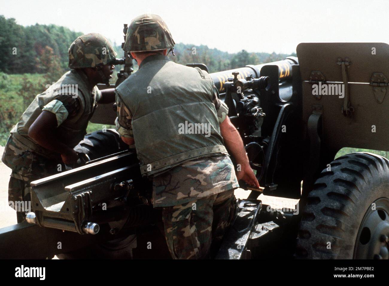 A right rear view of the gunner as he adjusts the sight of a 105mm ...