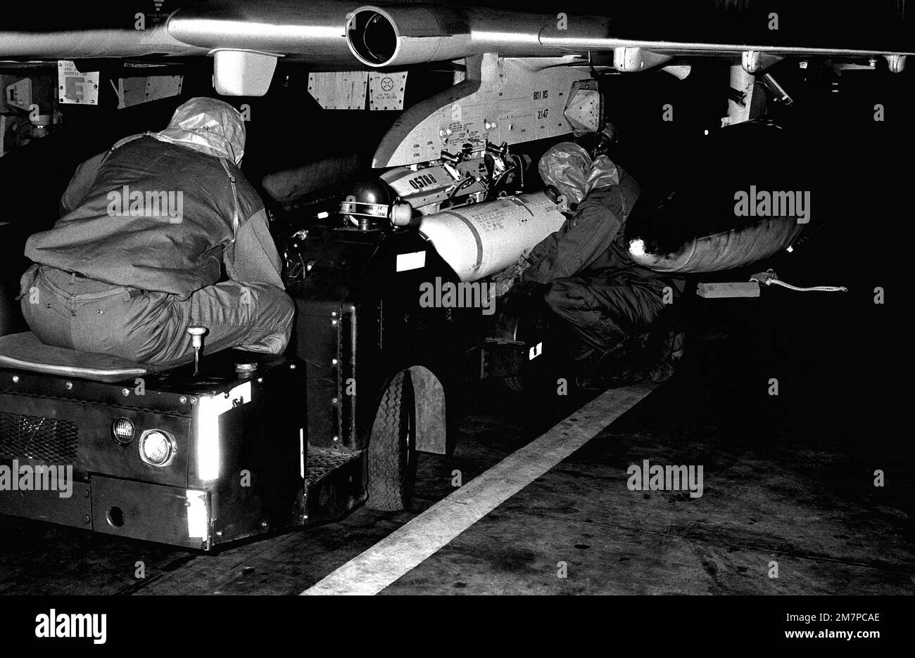 Airmen clad in protective chemical warfare gear demonstrate the loading ...