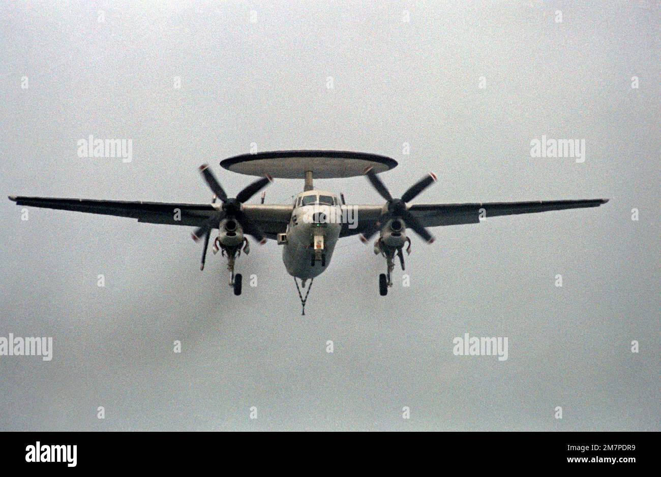 An E-2C Hawkeye aircraft, with its arresting hook down, approaches the ...