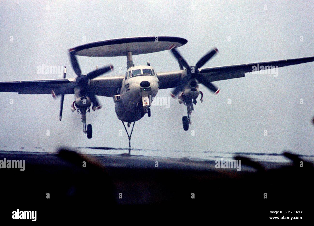 An E-2C Hawkeye aircraft, with its arresting hook down, approaches the ...