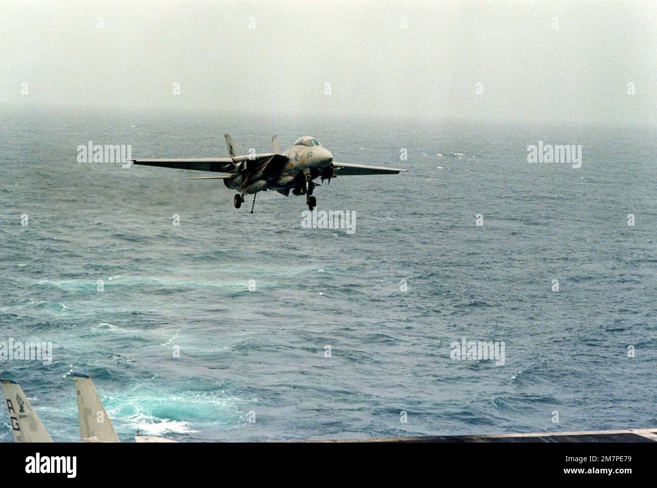 An F-14 Tomcat aircraft, with its arresting hook down, approaches for a ...