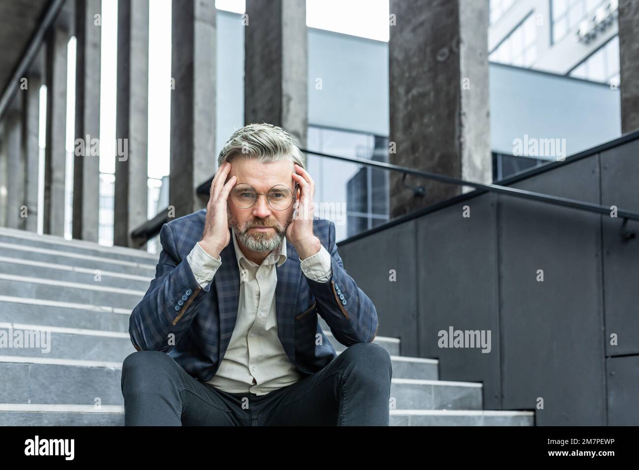 Gray haired businessman sitting sad on stairs outside office building ...