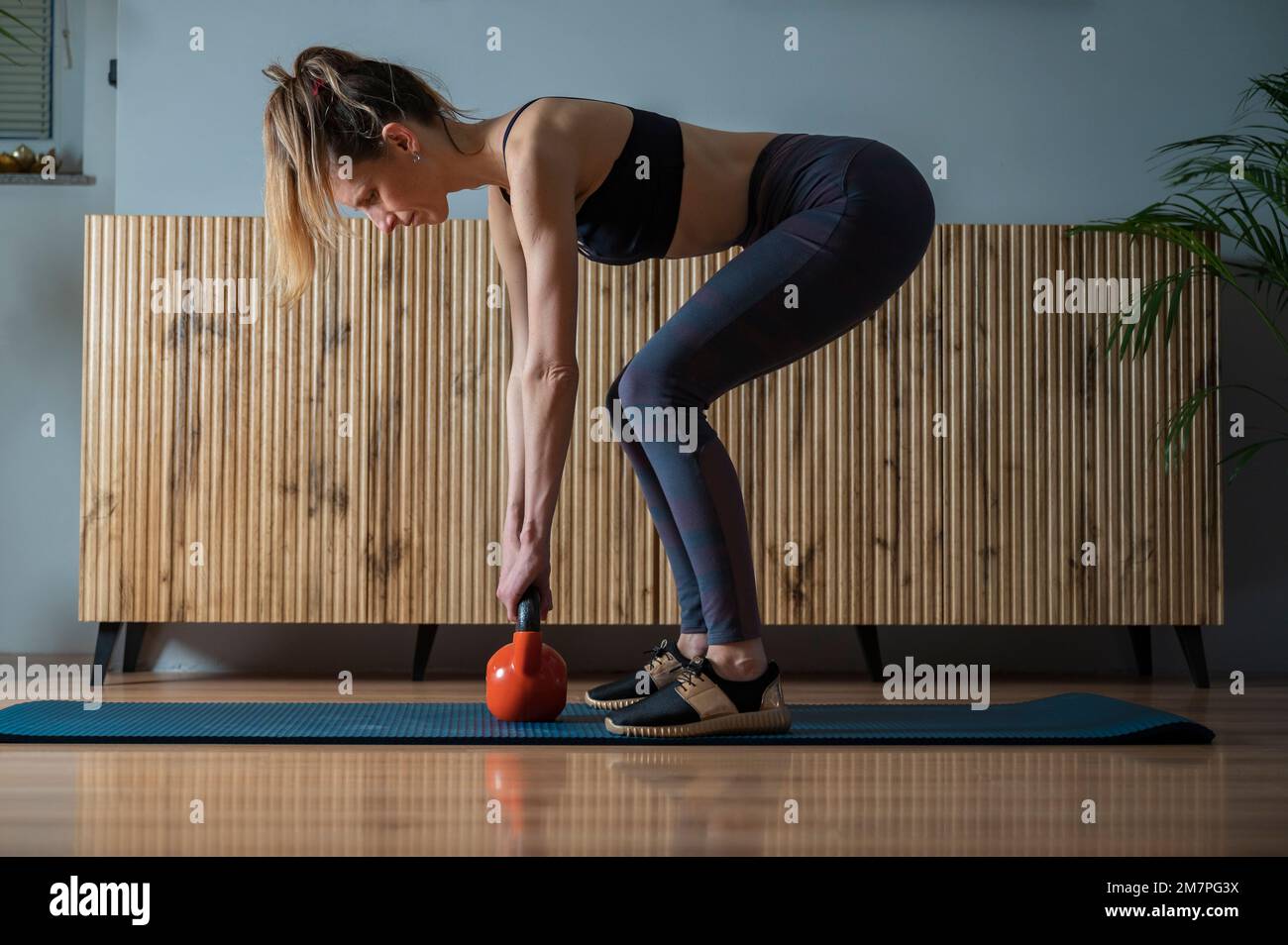 Side view of a woman working out at home making a deadlift exercise ...