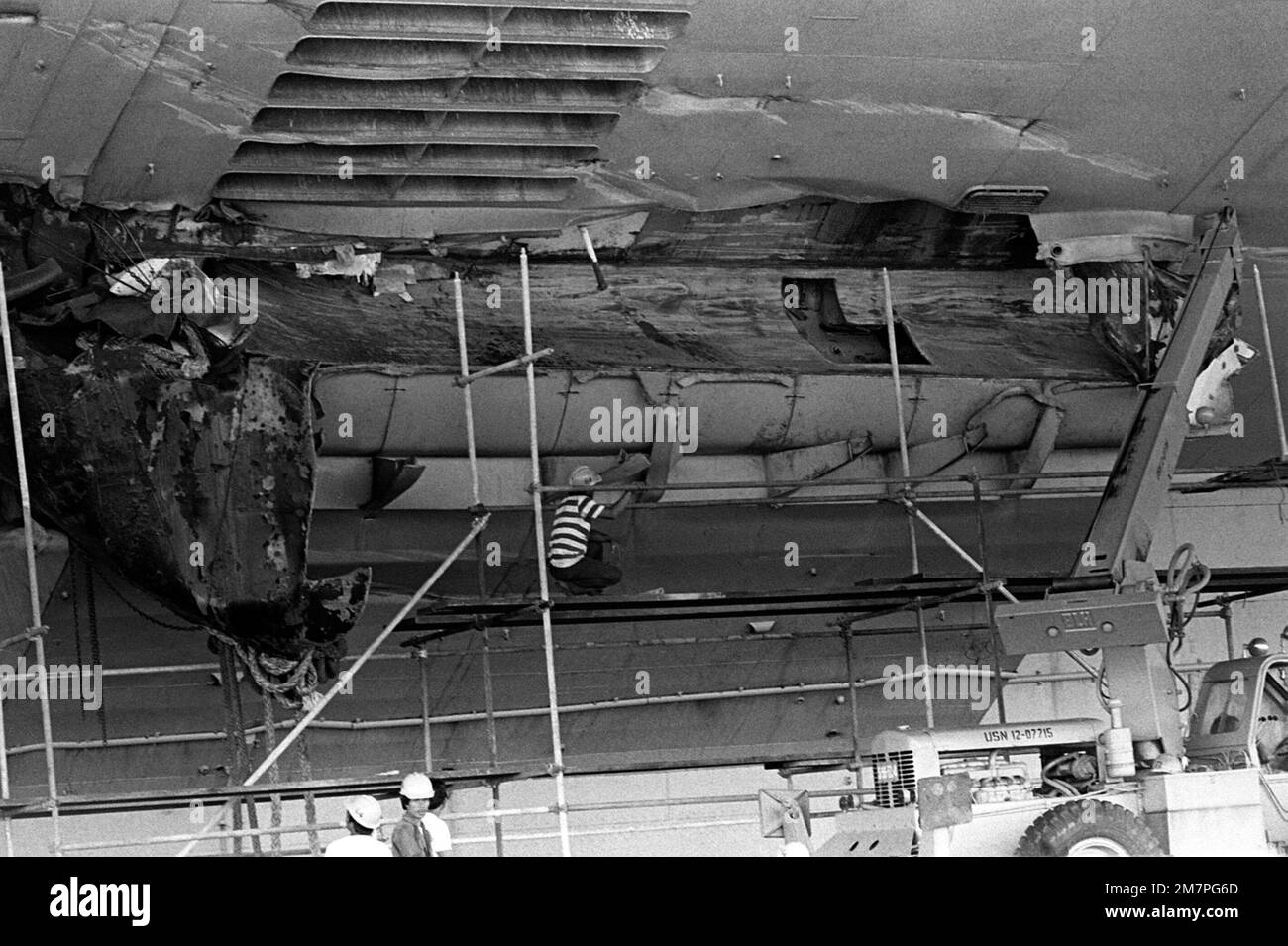 Workers aboard a barge make repairs to the port amidships section of ...