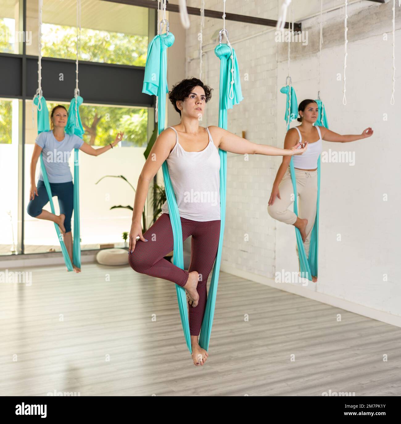 Slim young Latin woman using blue hammock for doing Vrksasana Tree Pose ...