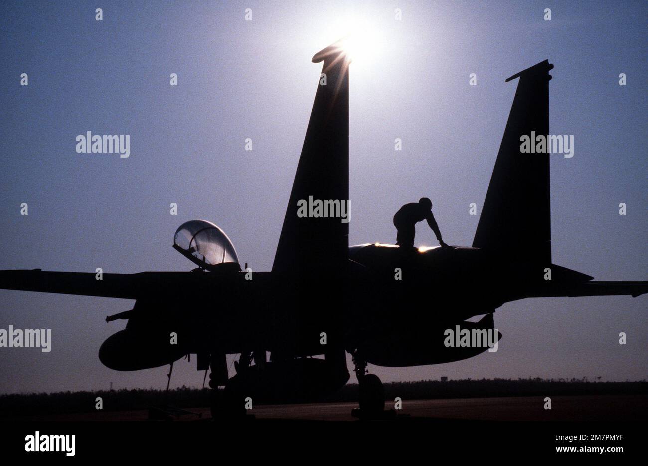 A view of a parked F-15 Eagle aircraft silhouetted against the sunset ...