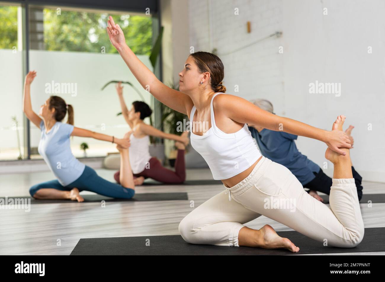 European young girl and group of active multinational women sitting on yoga mat and practicing ...