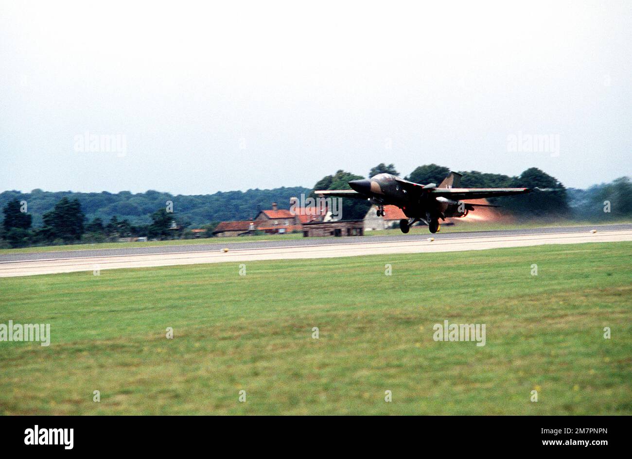 A left front view of an F-111 aircraft, with its after burner glowing ...