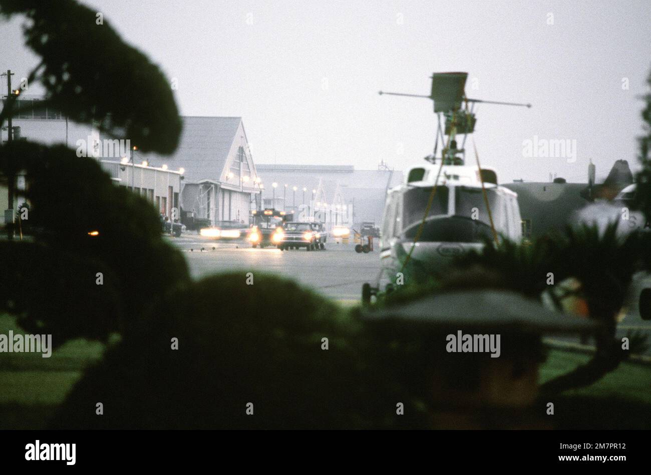 A morning view of the flight line framed by a plant and a close-up UH-1 ...