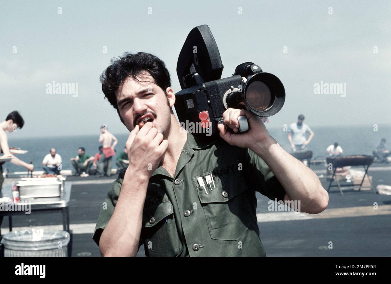 A photographer's mate takes a break from shooting motion picture film ...