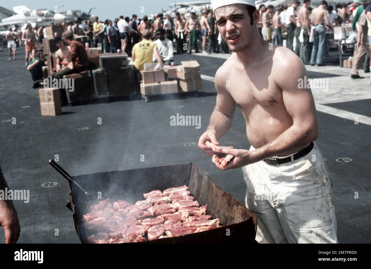 A mess management specialist grills steaks on the flight deck of the ...