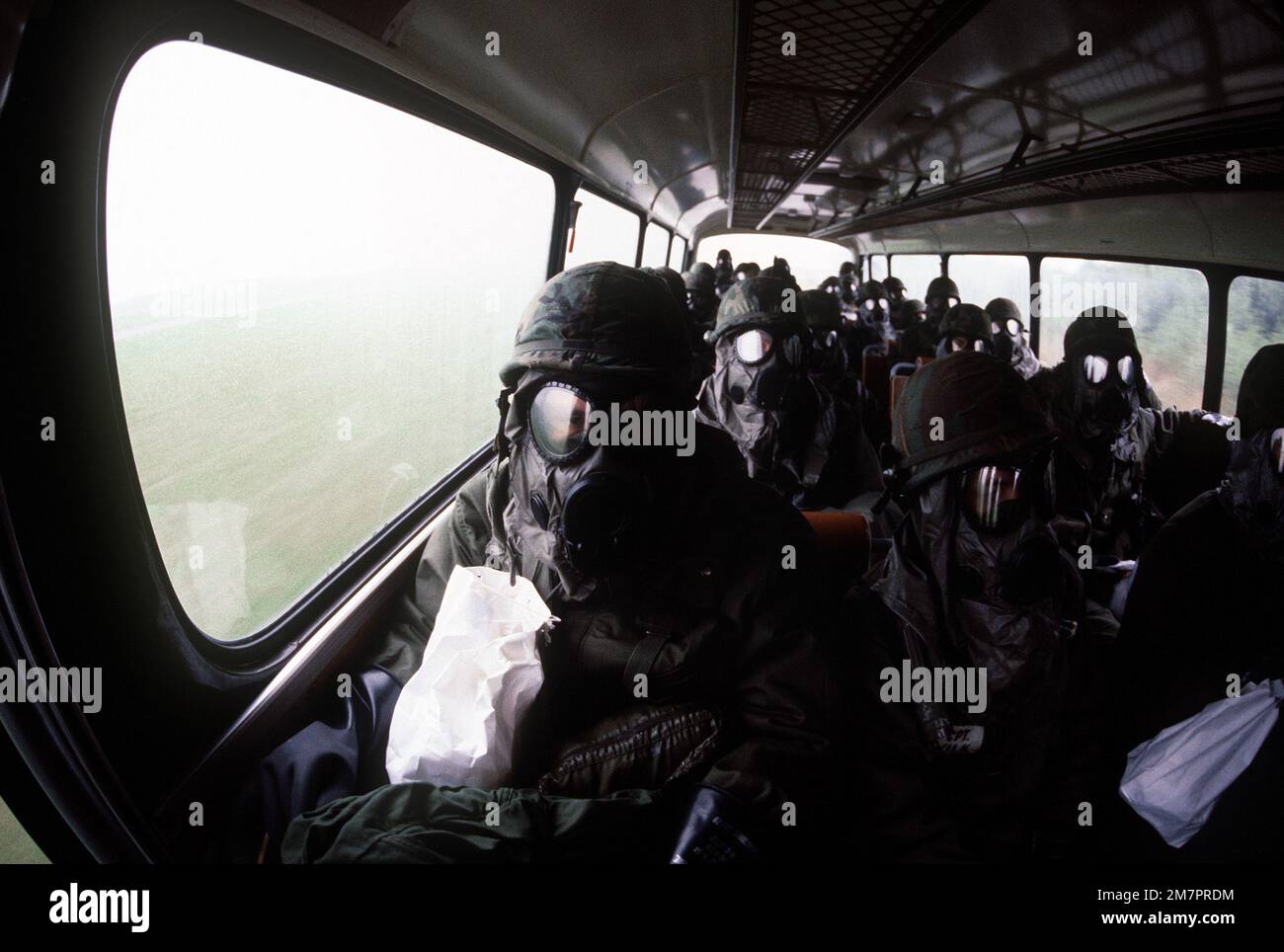 Troops wearing their chemical warfare gear ride a bus to an aircraft ...
