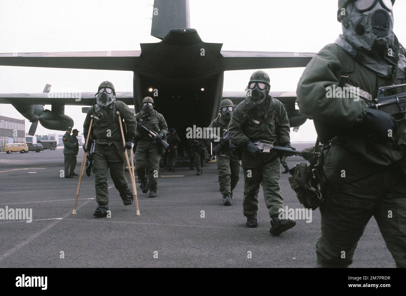 Troops, in chemical warfare gear and carrying M-16A1 rifles, march down ...