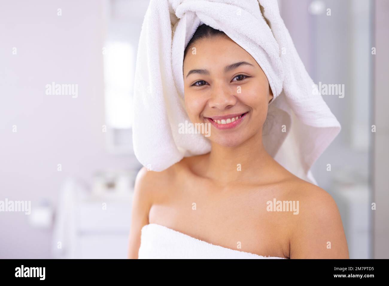 Portrait of happy biracial woman wearing towel smiling in bathroom ...