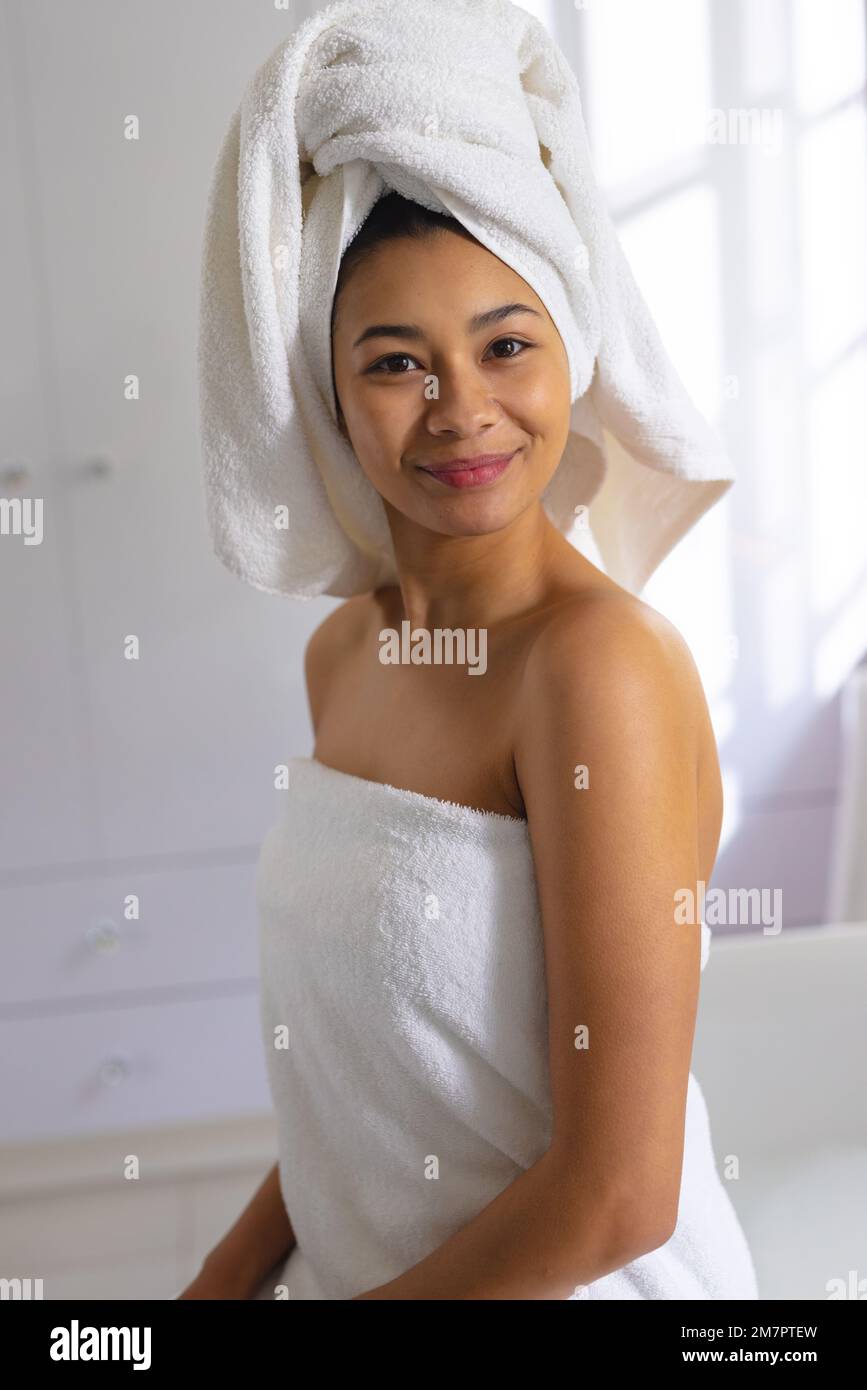 Vertical portrait of happy biracial woman wearing towel, smiling in ...