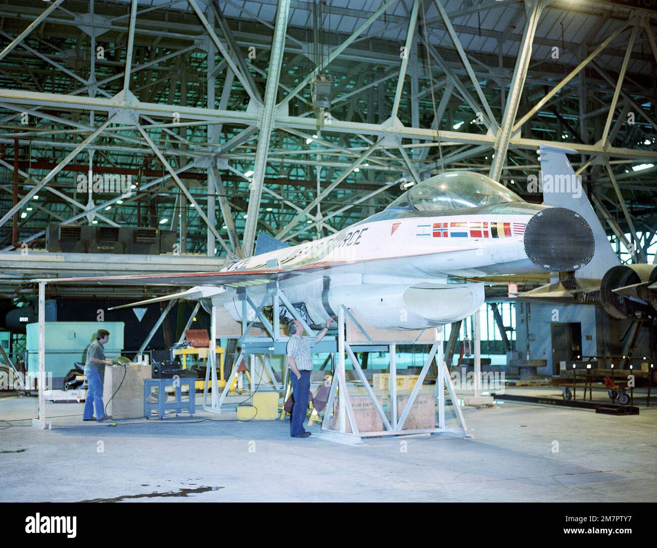 Workmen inspect the fuselage of a YF-16 Eagle aircraft upon its arrival ...