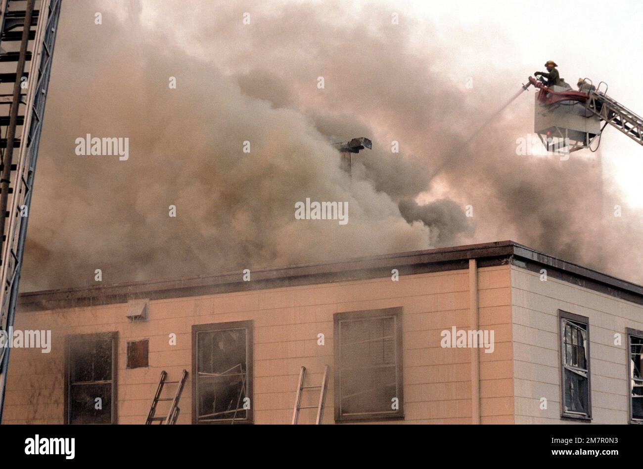 Firemen, on a fire-engine tower ladder, fight a fire, which is burning ...