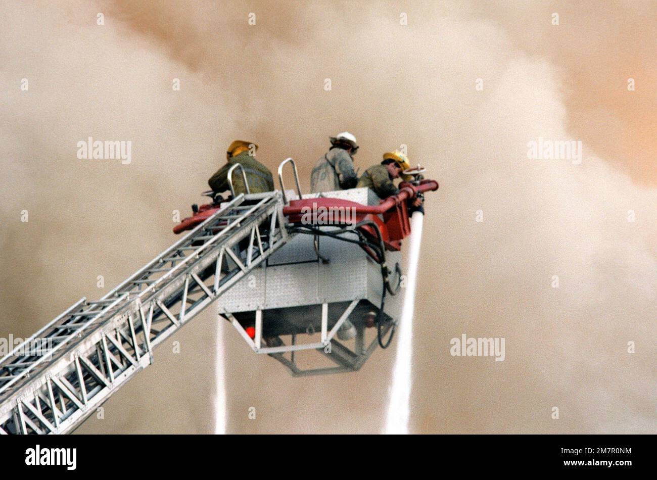 Firemen, on a fire-engine tower ladder, fight a fire, which is burning ...