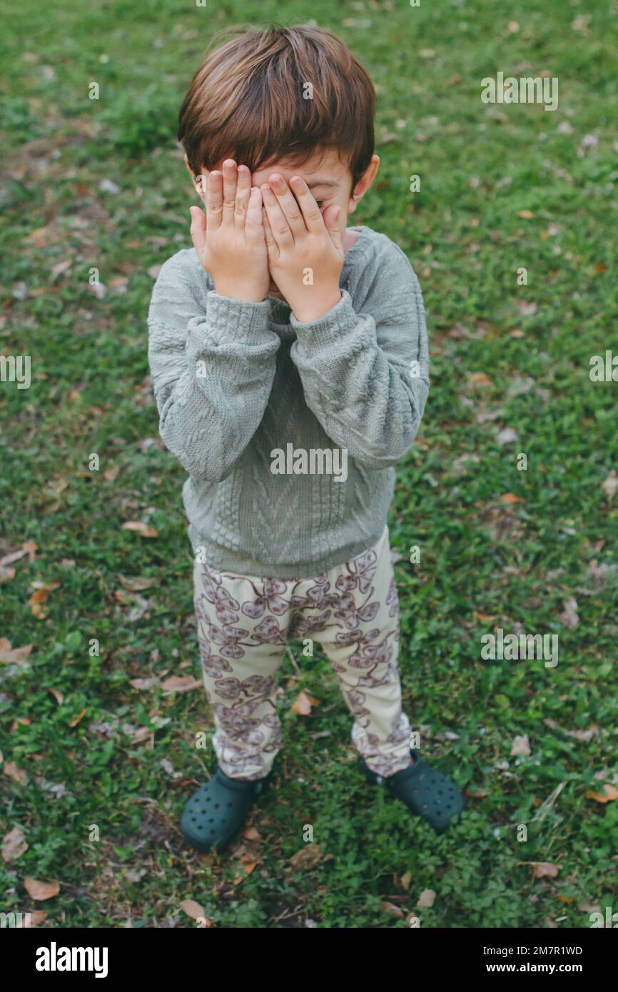 Little boy covering face with hands in backyard on St Patrick's Day ...