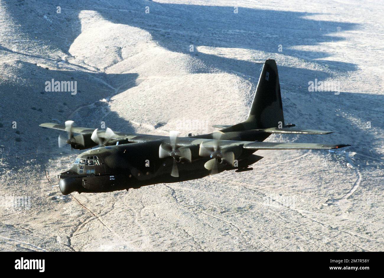 AN air-to-air left side view of an MC-130E Hercules aircraft flying low ...