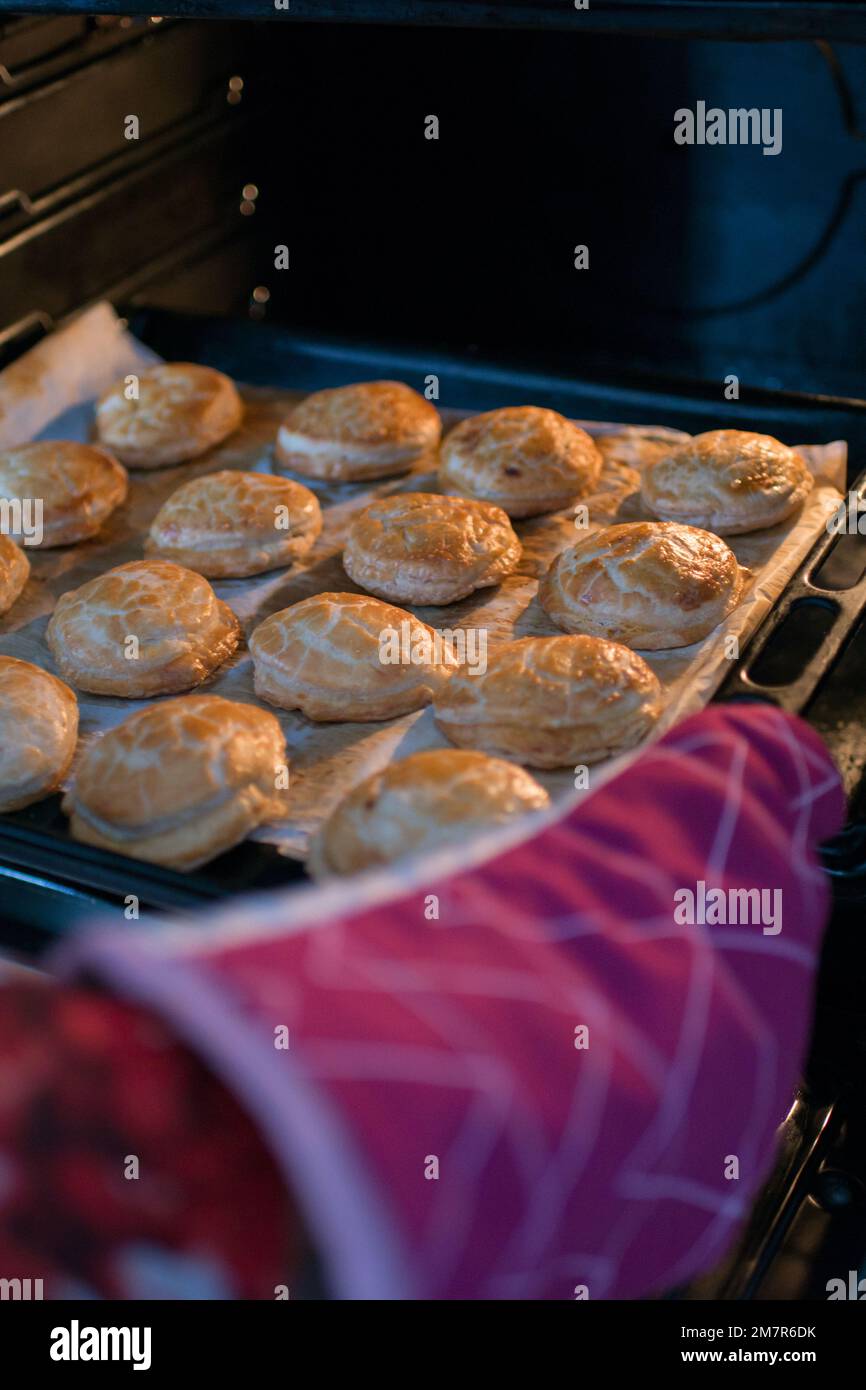 Human hand with an oven glove taking out of the oven a tray with pastry ...