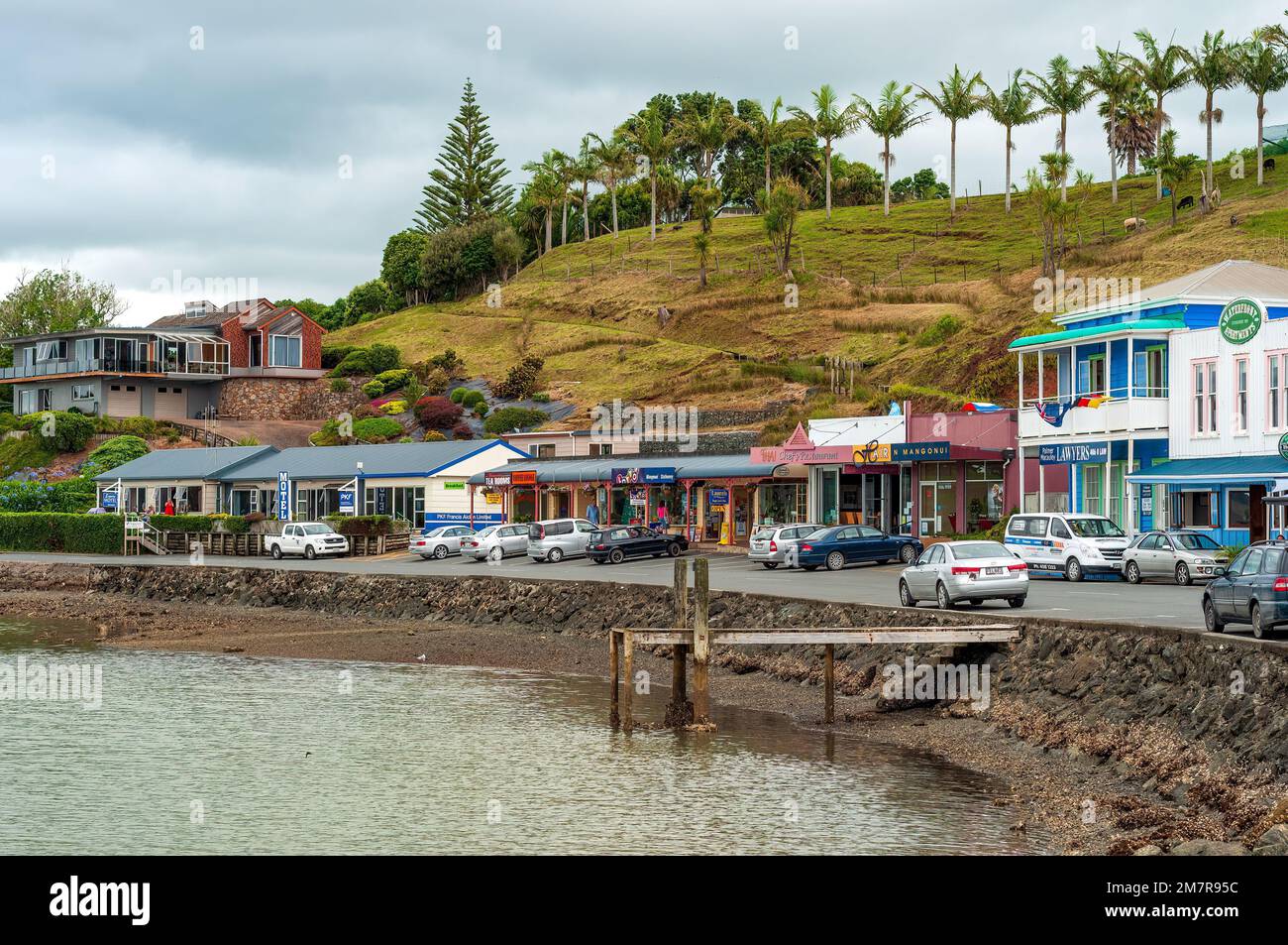 A scenic view of cars parked on the waterfront road in front of shops ...