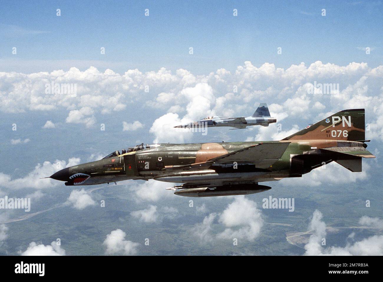 AN air-to-air left side view of an F-4E Phantom II aircraft, foreground, and an F-5E Tiger II ...