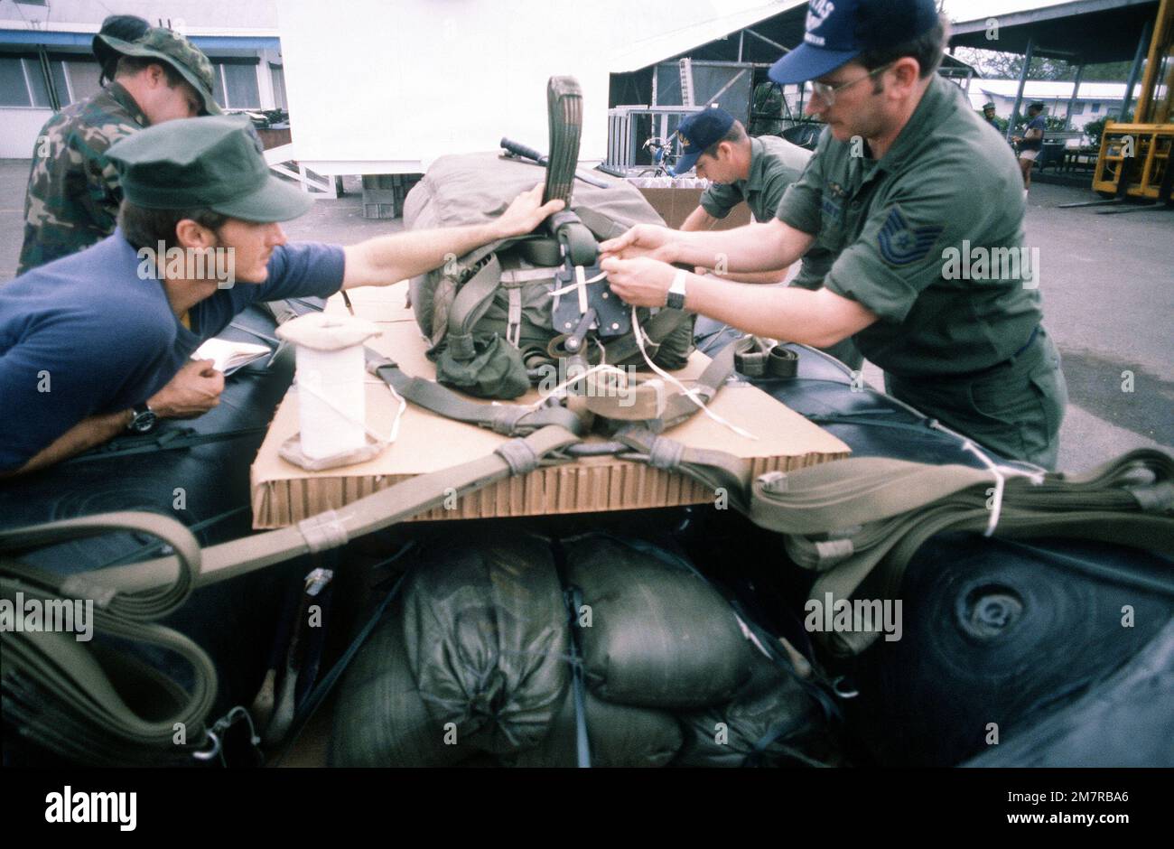 Military personnel secure a parachute to the top of a packed rubber ...