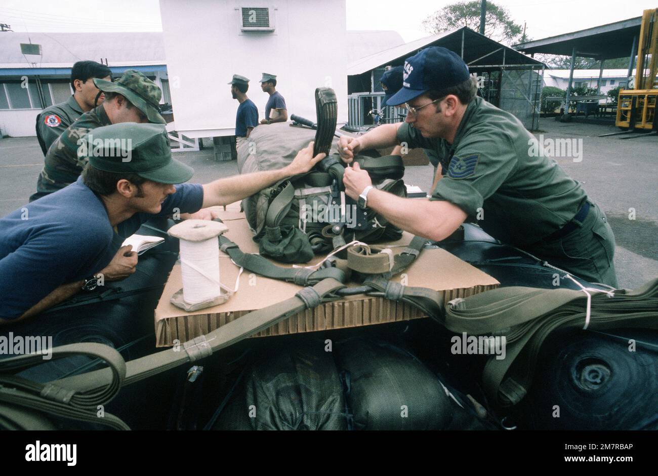 Military personnel secure a parachute to the top of a packed rubber ...