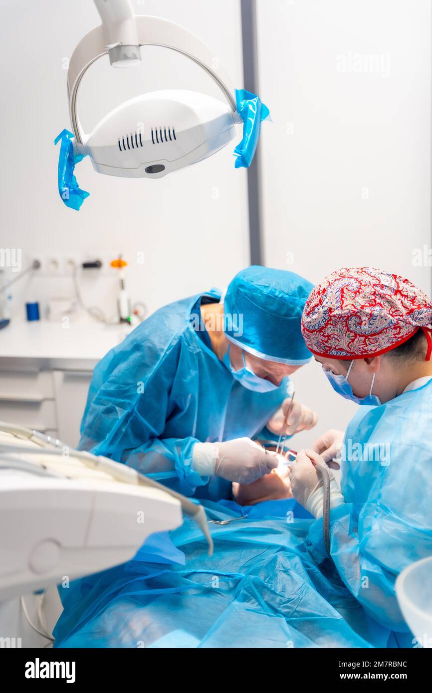 Female dentists in blue scrubs performing a complicated operation on a ...