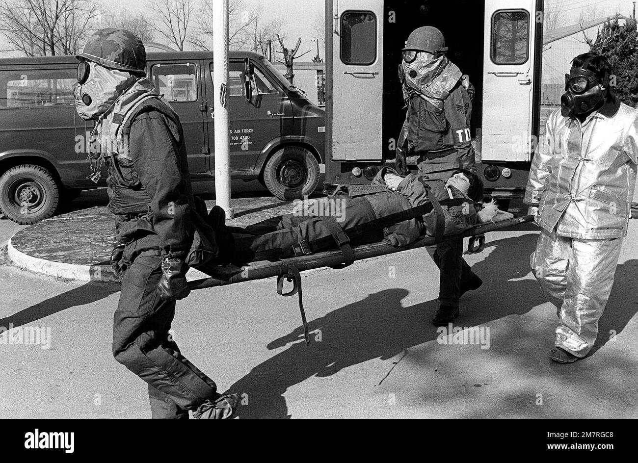 Air Force members, wearing chemical warfare gear, carry a "patient ...